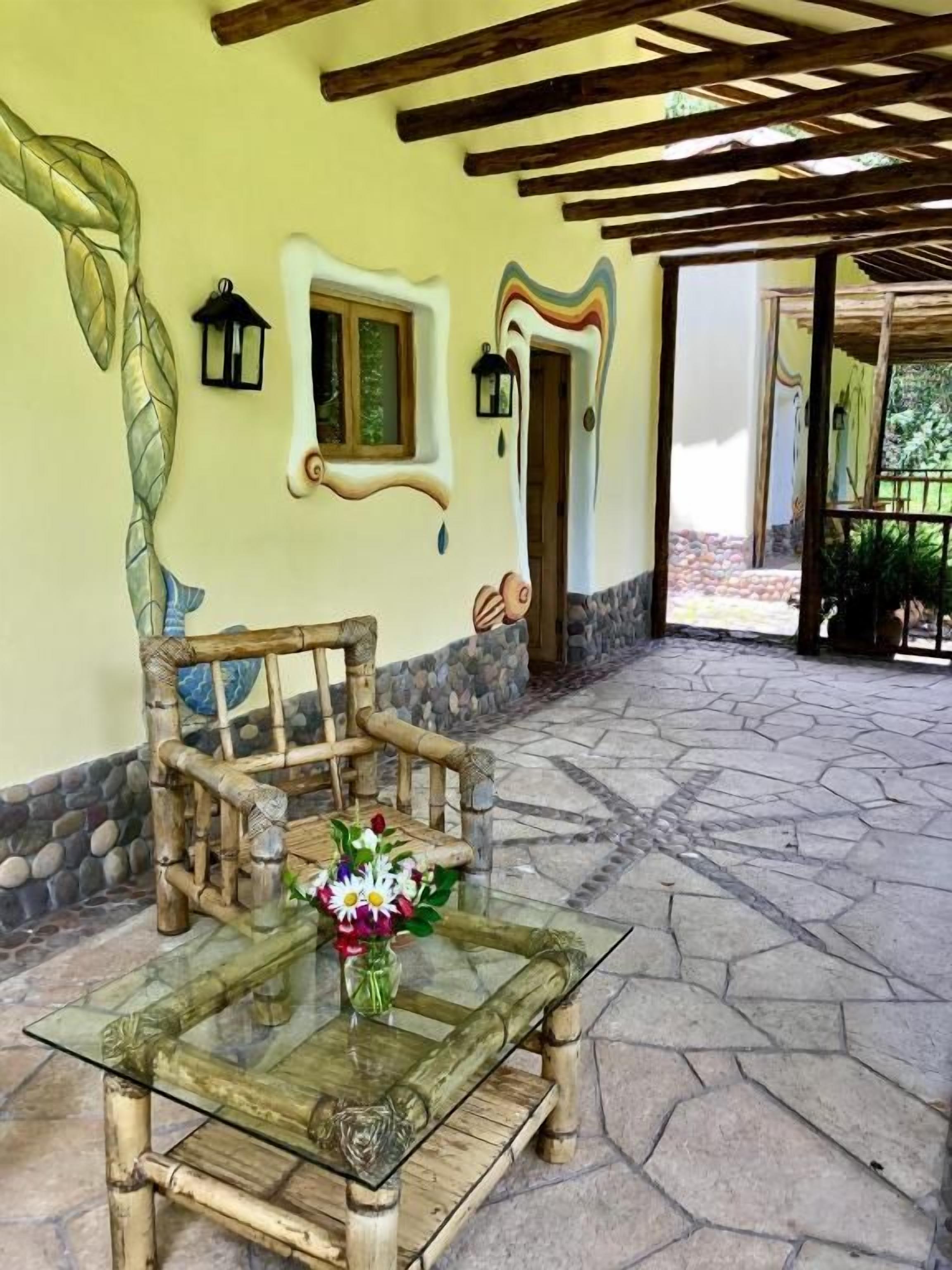 Quarto com mesa de centro de vidro, uma cadeira de madeira e parede decorativa com motivos de folhas.
