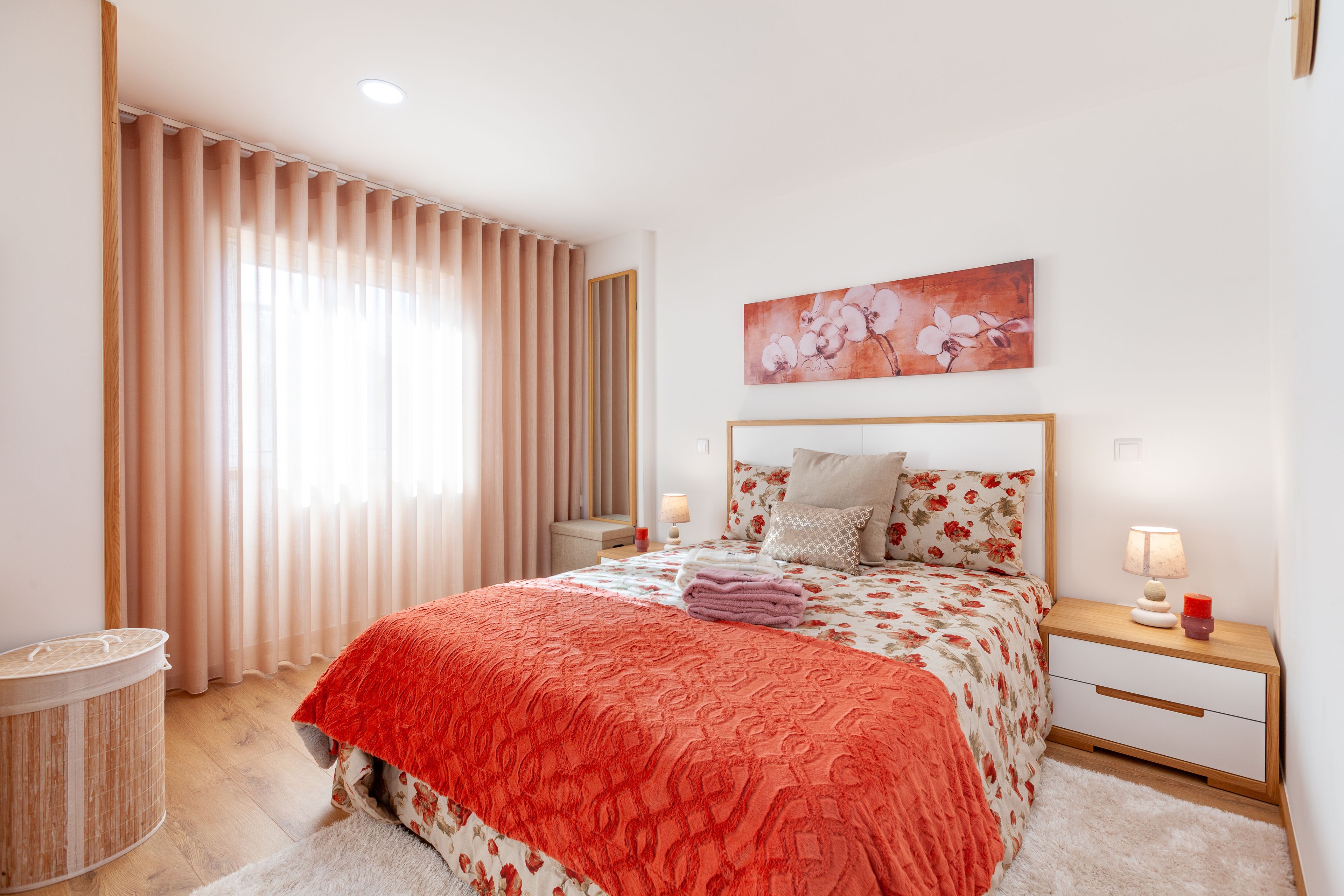 Quarto com cama, cortinas, mesa de cabeceira, abajur e um quadro na parede.