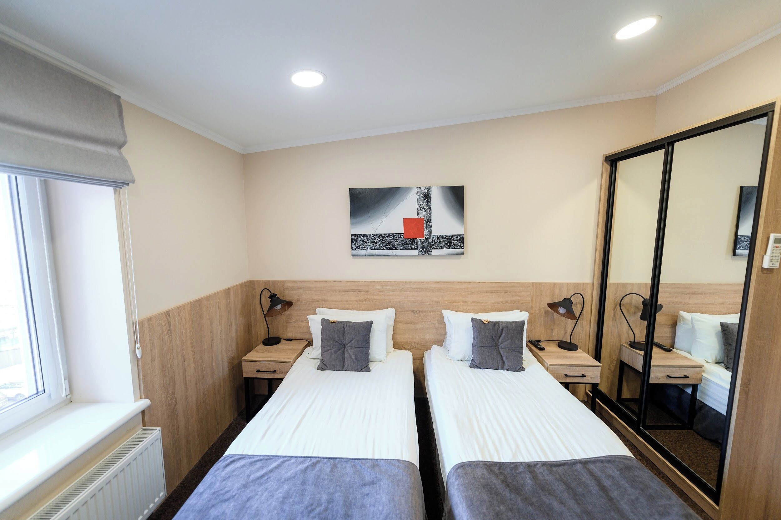 Quarto de hotel com duas camas de solteiro, um espelho grande, um quadro na parede e uma janela com persianas.