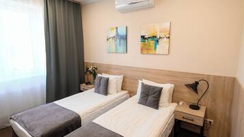 Quarto de hotel com duas camas, uma mesa de cabeceira com abajur, ar-condicionado e dois quadros na parede.