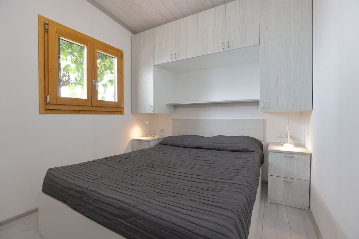 Quarto com cama, duas mesas de cabeceira, uma janela e armários embutidos.