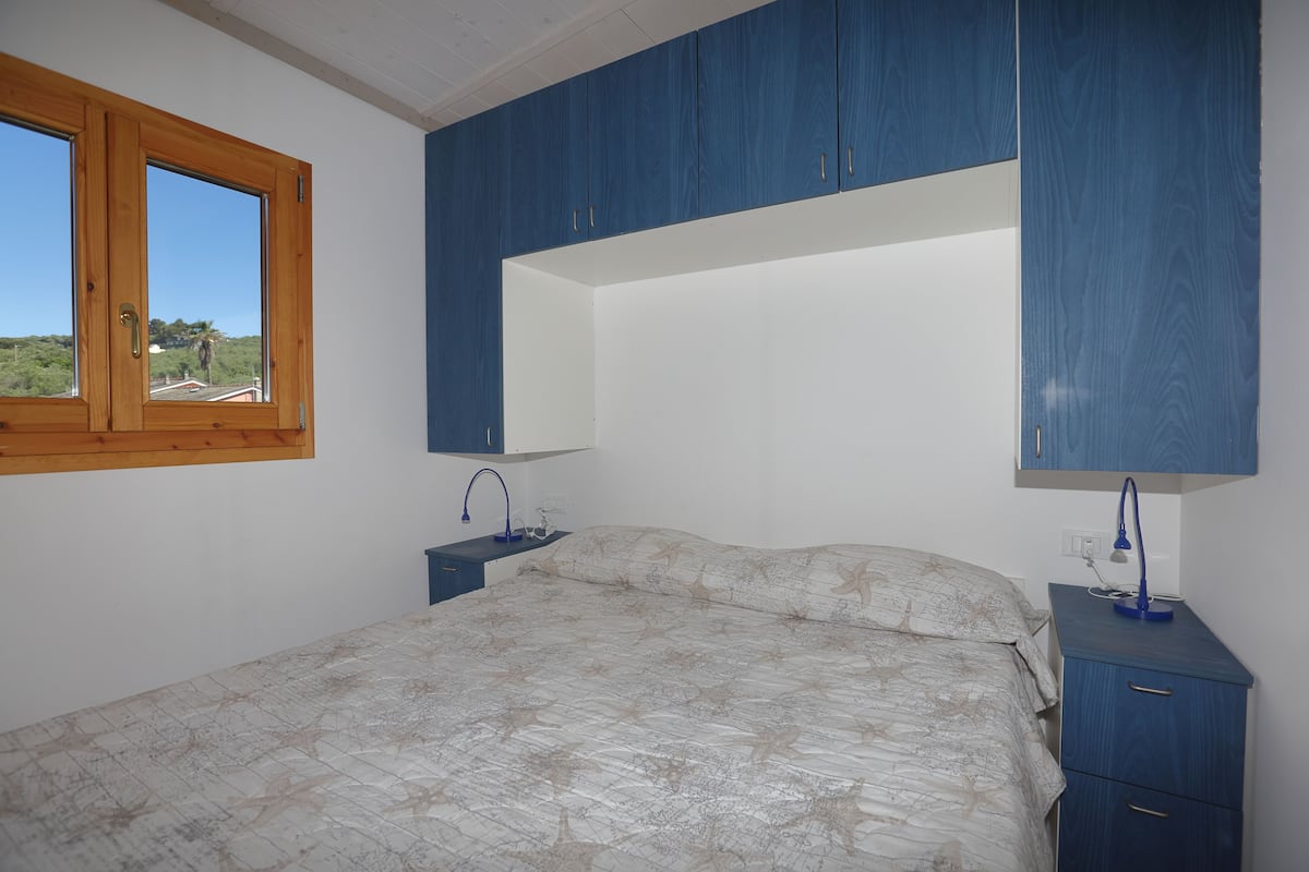 Quarto com cama, mesa de cabeceira, escrivaninha e janela.