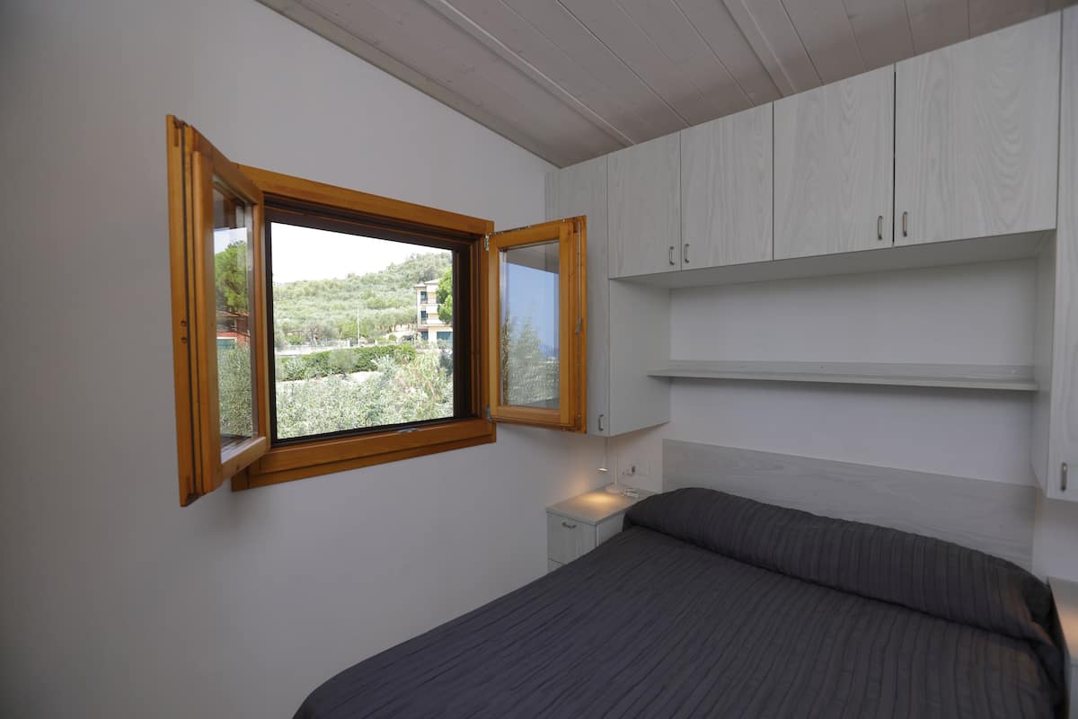 Quarto com cama, mesa de cabeceira, janela com moldura de madeira e armários brancos.