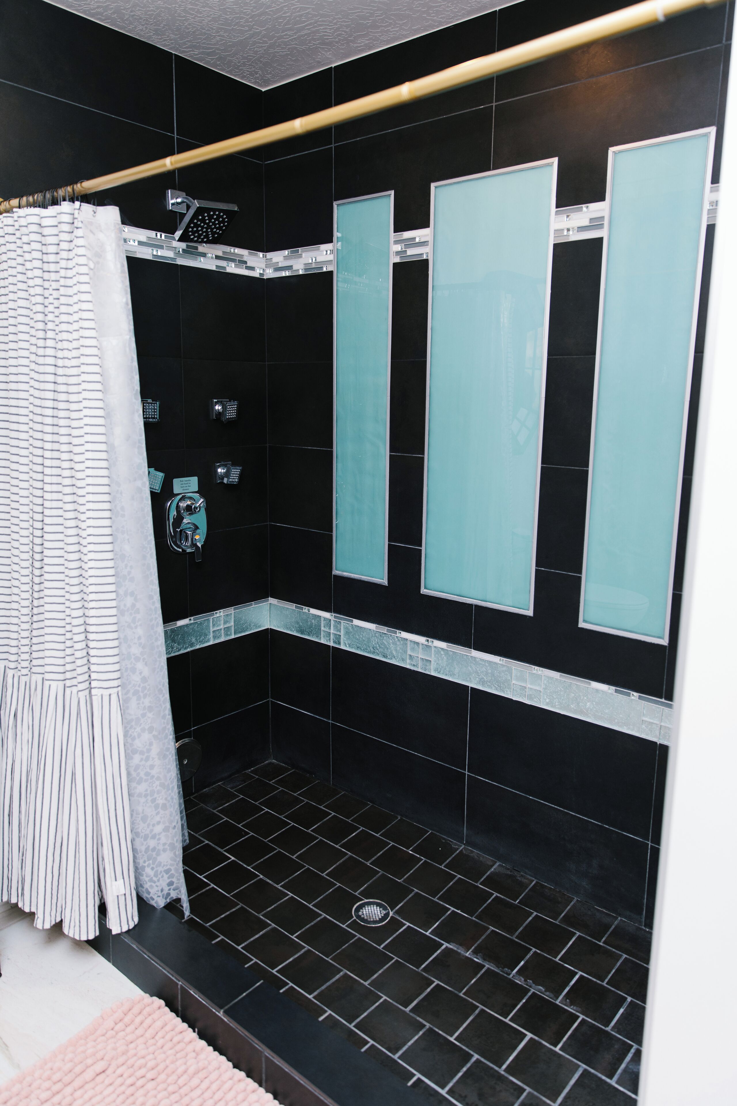 Um banheiro moderno com azulejos pretos, chuveiro com barra de bambu e box de vidro.