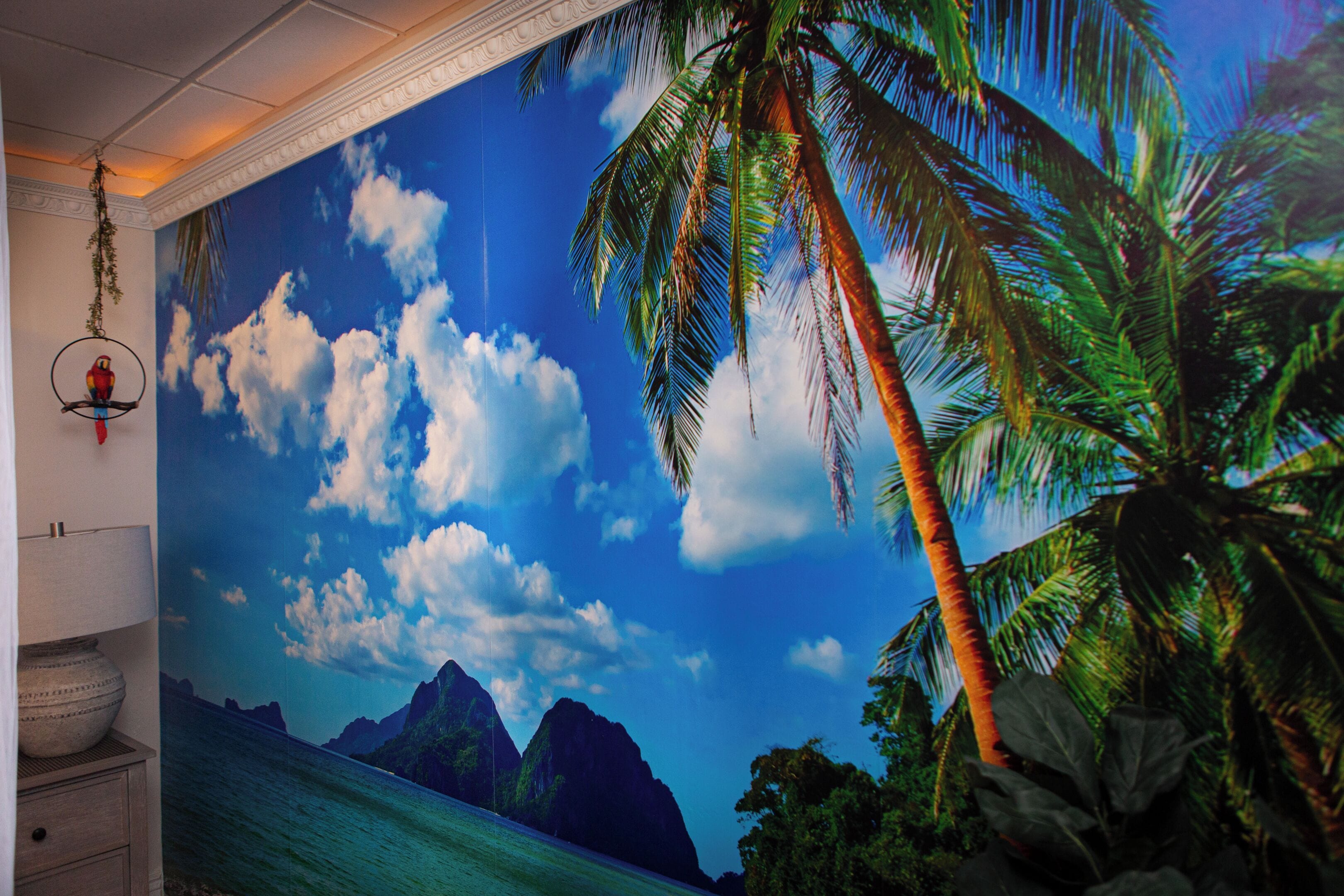 Quarto com um mural de paisagem tropical, planta pendente e mesa de cabeceira com abajur.