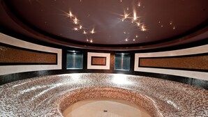Uma grande área de hidromassagem circular, com paredes e teto revestidos em mosaico.
