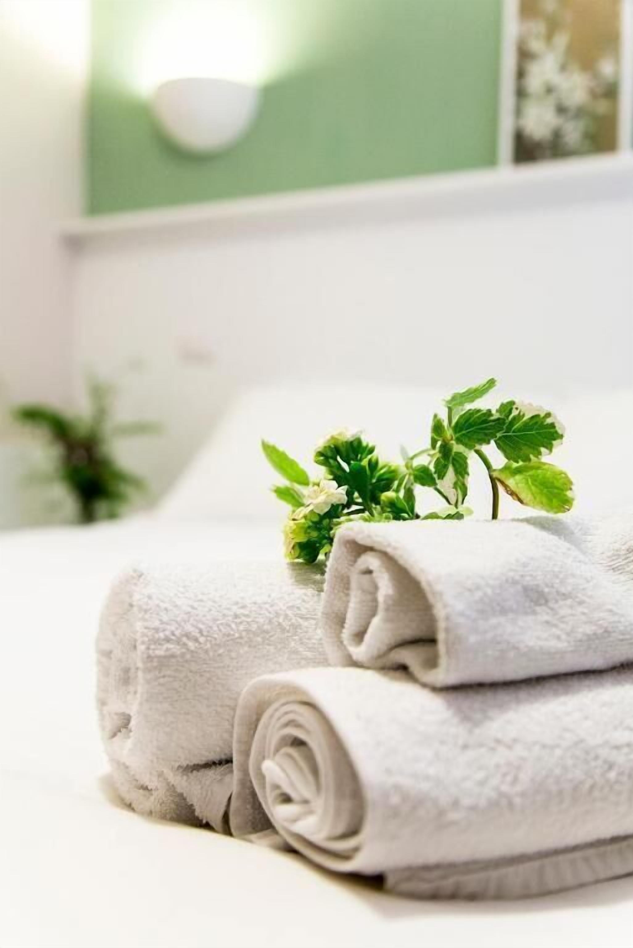 Toalha branca dobrada cuidadosamente sobre uma cama, com parede verde e parede branca ao fundo.