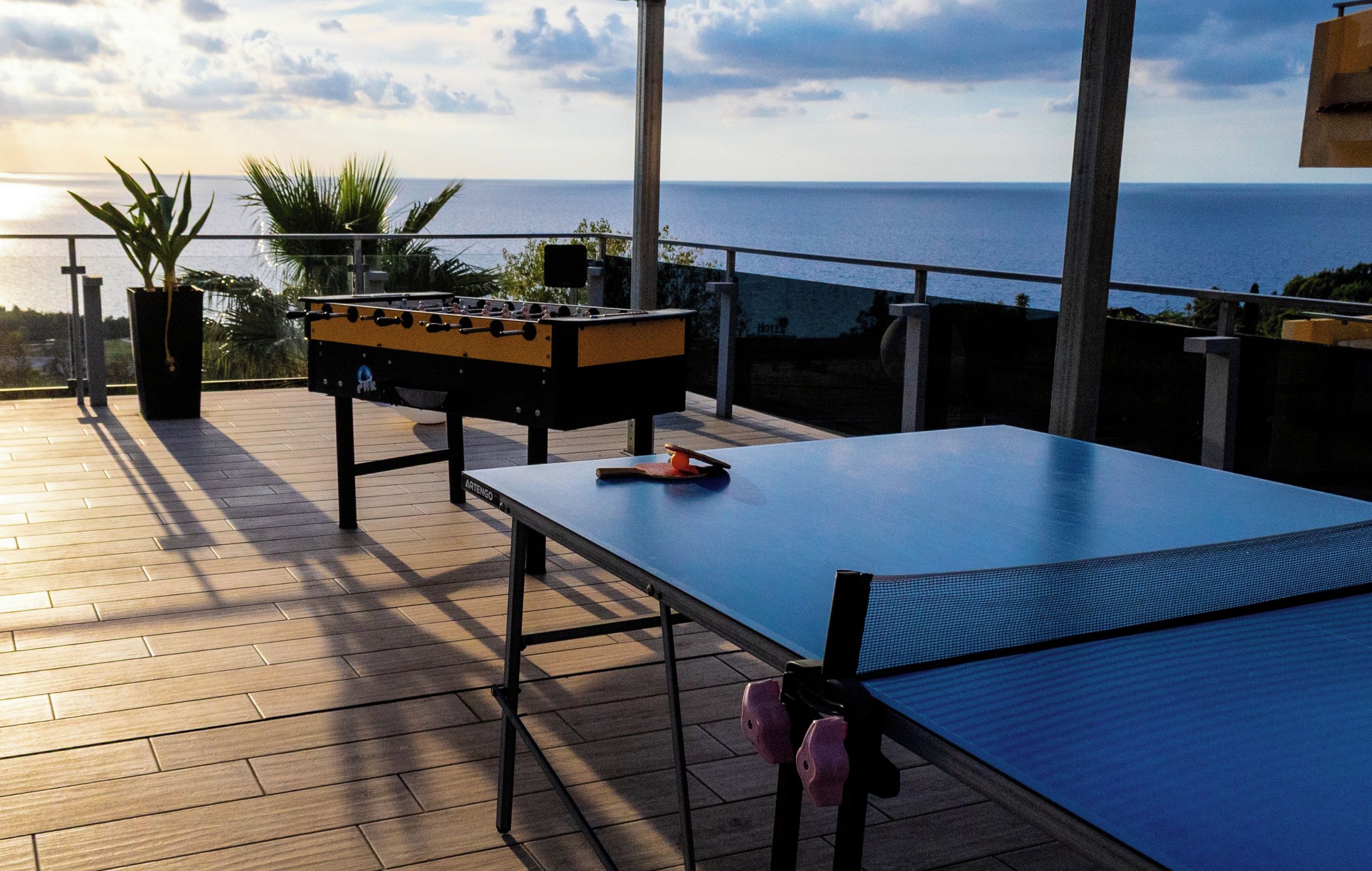 Mesa de pebolim e mesa de pingue-pongue em um deck ao ar livre, com vista para o mar.