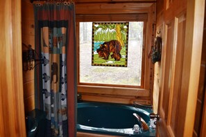 Casa de banho de cabana de madeira com banheira, janela de vitrais representando um urso e cortina com padrões de animais.