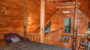 Interior de uma cabana de madeira com uma cama, uma mesa de jantar e uma escada para um andar superior.