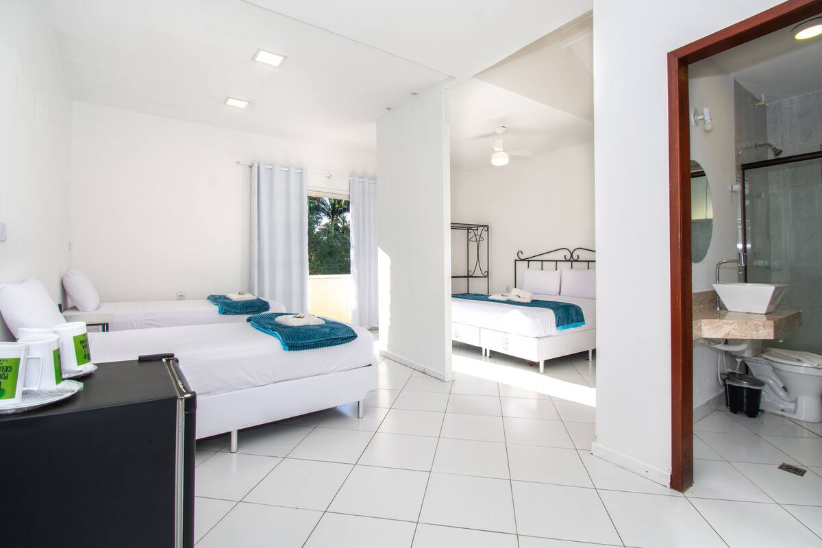 Quarto de hotel com duas camas, banheiro e uma pequena mesa com xícaras.