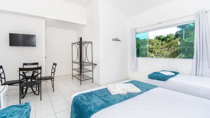 Quarto de hotel com cama, escrivaninha, cadeira, televisão e janela com vista para área verde.