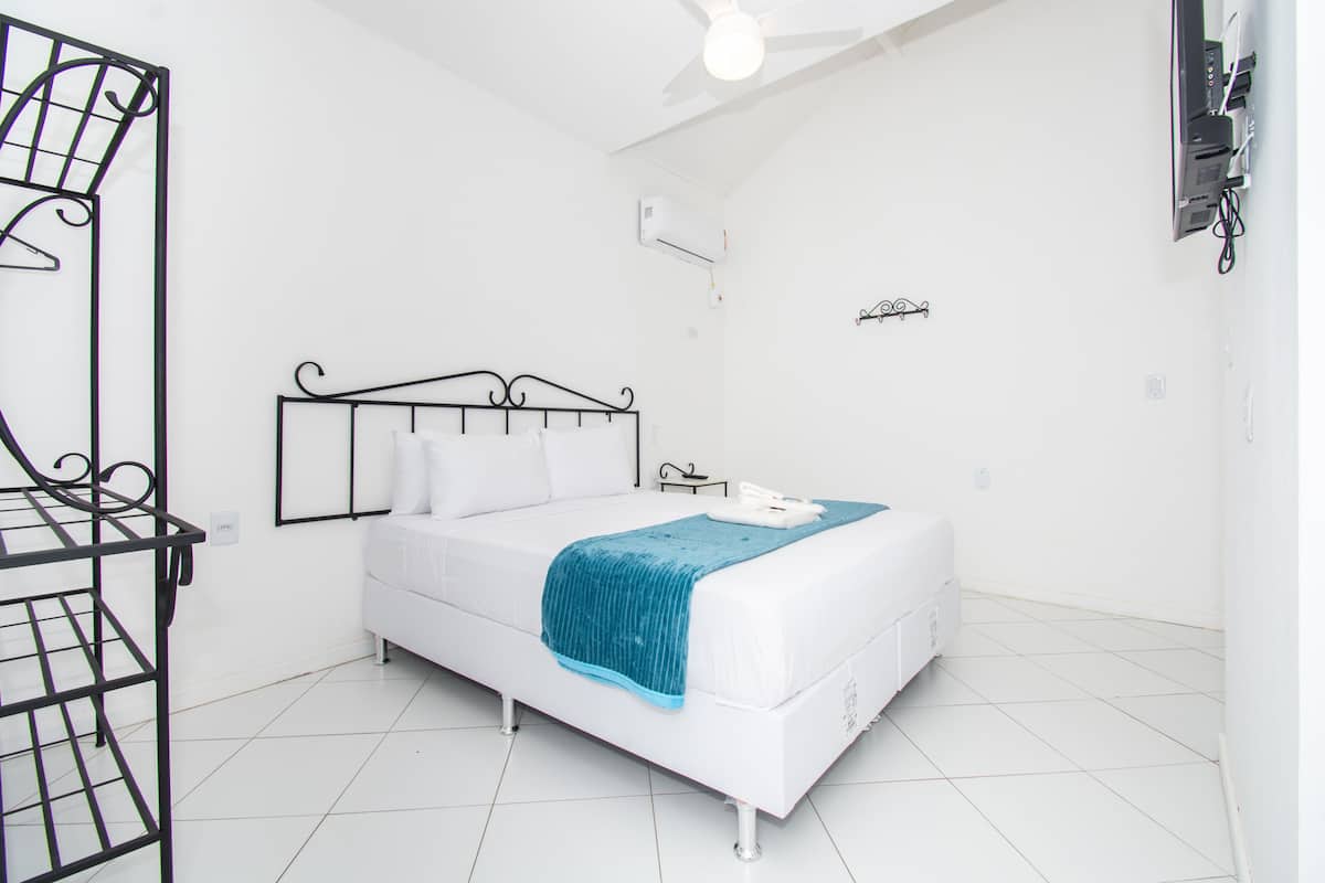 Um quarto branco com uma cama, um ventilador de teto e um ar condicionado fixado na parede.