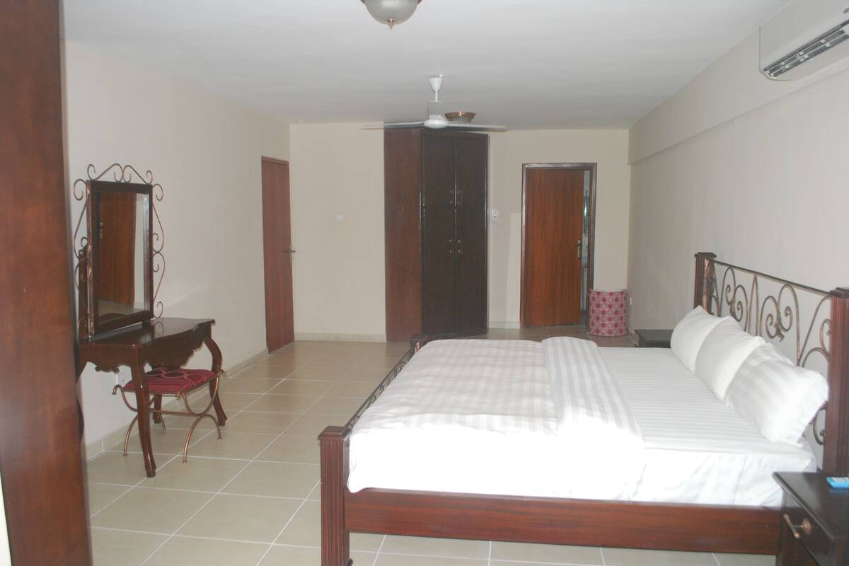 Quarto com uma cama grande, cômoda de madeira, espelho e ventoinha no teto.