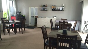 Uma área de refeições com mesa, cadeiras, geladeira e prateleiras com utensílios de cozinha.