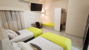 Quarto de hotel com duas camas de solteiro, uma mesa com cadeira, televisão na parede e um guarda-roupa pequeno.