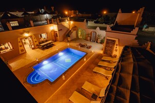 Uma área de piscina no terraço, com piscina azul, espreguiçadeiras e escadaria para um andar superior.