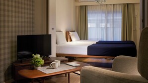 Quarto de hotel com cama, televisão, escrivaninha com planta e uma cadeira.