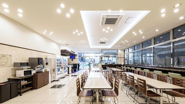 Uma cafeteria moderna com mesas e cadeiras compridas, máquinas de venda automática e uma grande janela com vista para o exterior.
