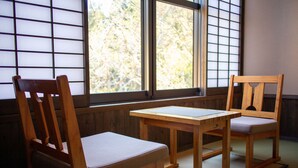 Um quarto japonês tradicional com tatames, uma mesa de madeira baixa e duas cadeiras de madeira.