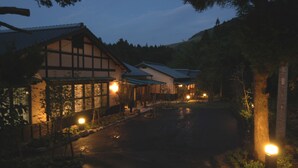 Um ryokan japonês tradicional, com quartos de tatame, fachada de madeira e um jardim com lago de carpas.