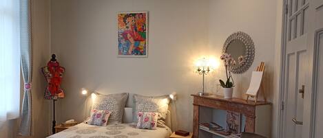 Quarto bem arrumado com cama, mesas de cabeceira, cômoda, cadeira e espelho fixado na parede.