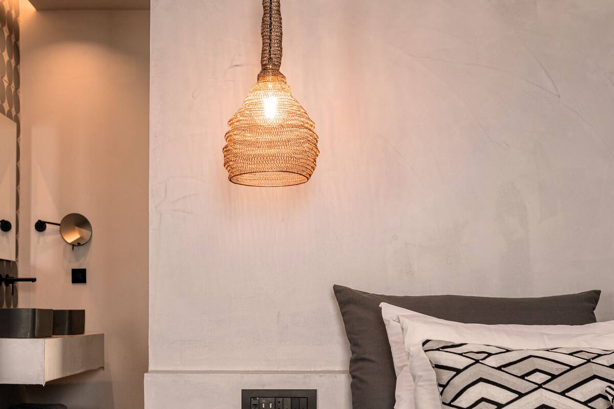 Quarto moderno com luminária pendente, cama com roupa de cama listrada e mesa de cabeceira com um livro e chinelos.
