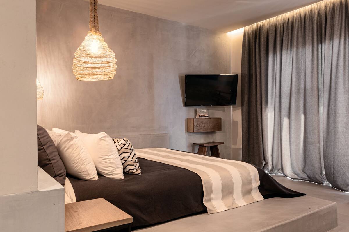 Quarto moderno com cama, televisão e uma janela grande com cortinas.
