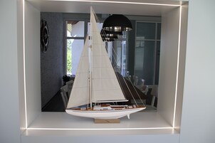 Um modelo de veleiro exibido em uma sala moderna e bem iluminada, com parede de tijolos e grandes janelas.