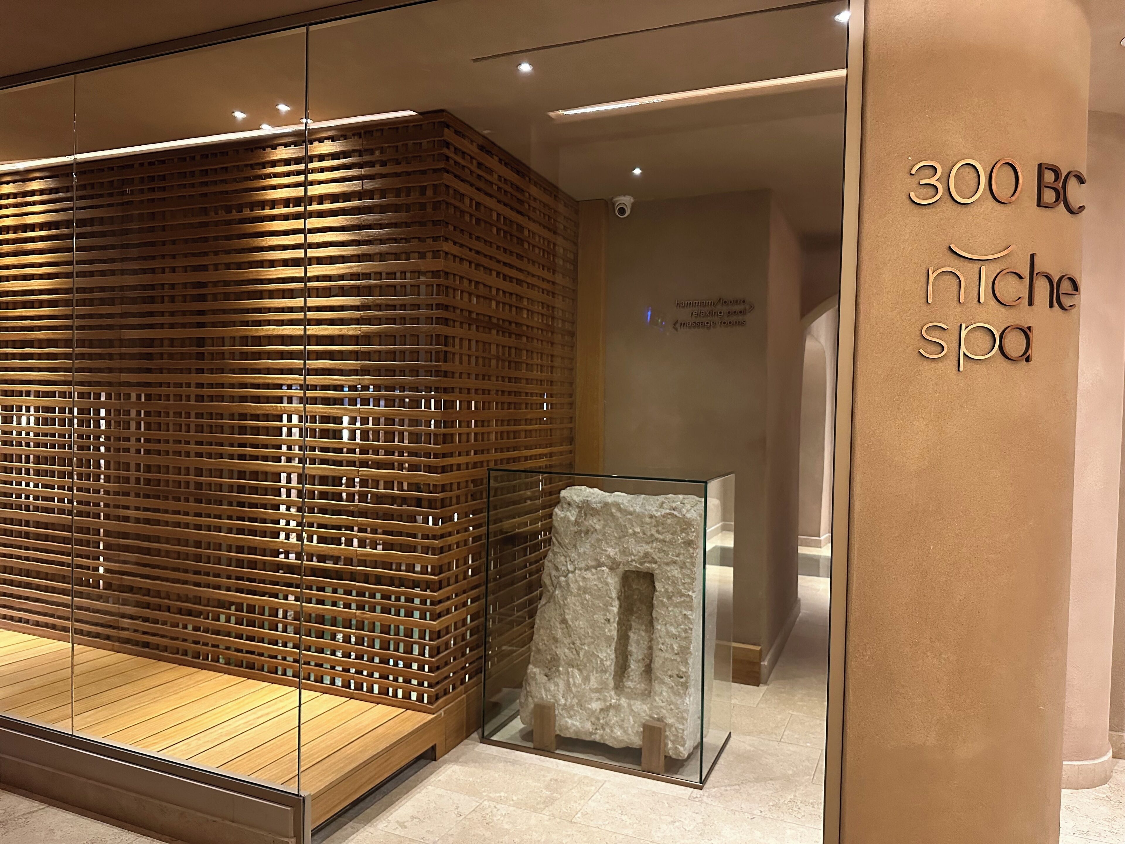 Entrada de um spa com parede de treliça de madeira, vitrine de vidro e placa indicando "300 BC niche spa".