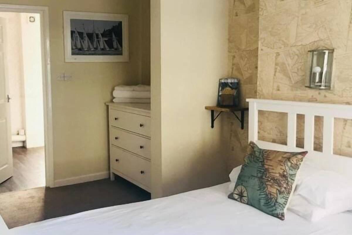 Quarto com cama, penteadeira, prateleira fixada na parede com abajur e quadro na parede.