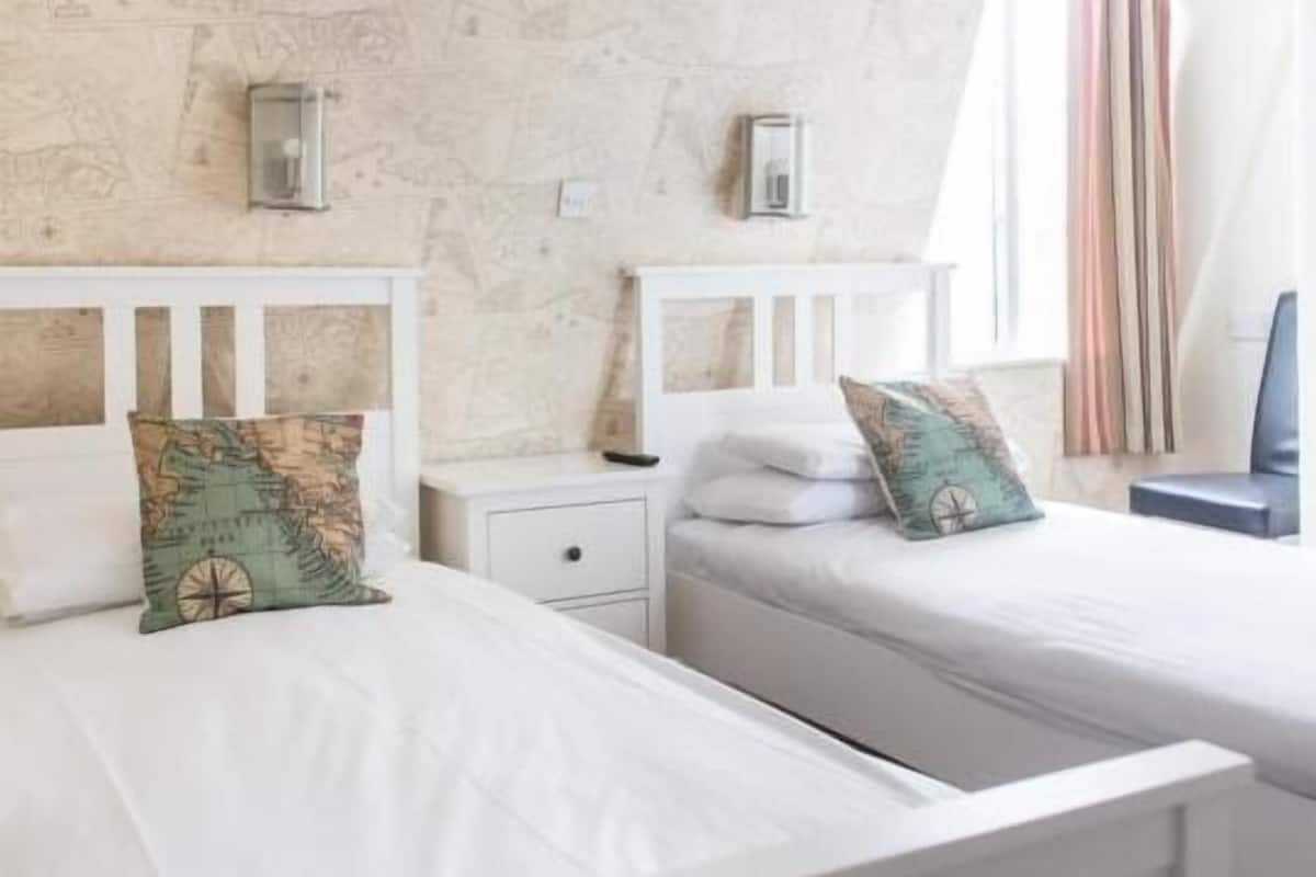Quarto com duas camas de solteiro, cada uma com cabeceira branca e almofada com tema de mapa.