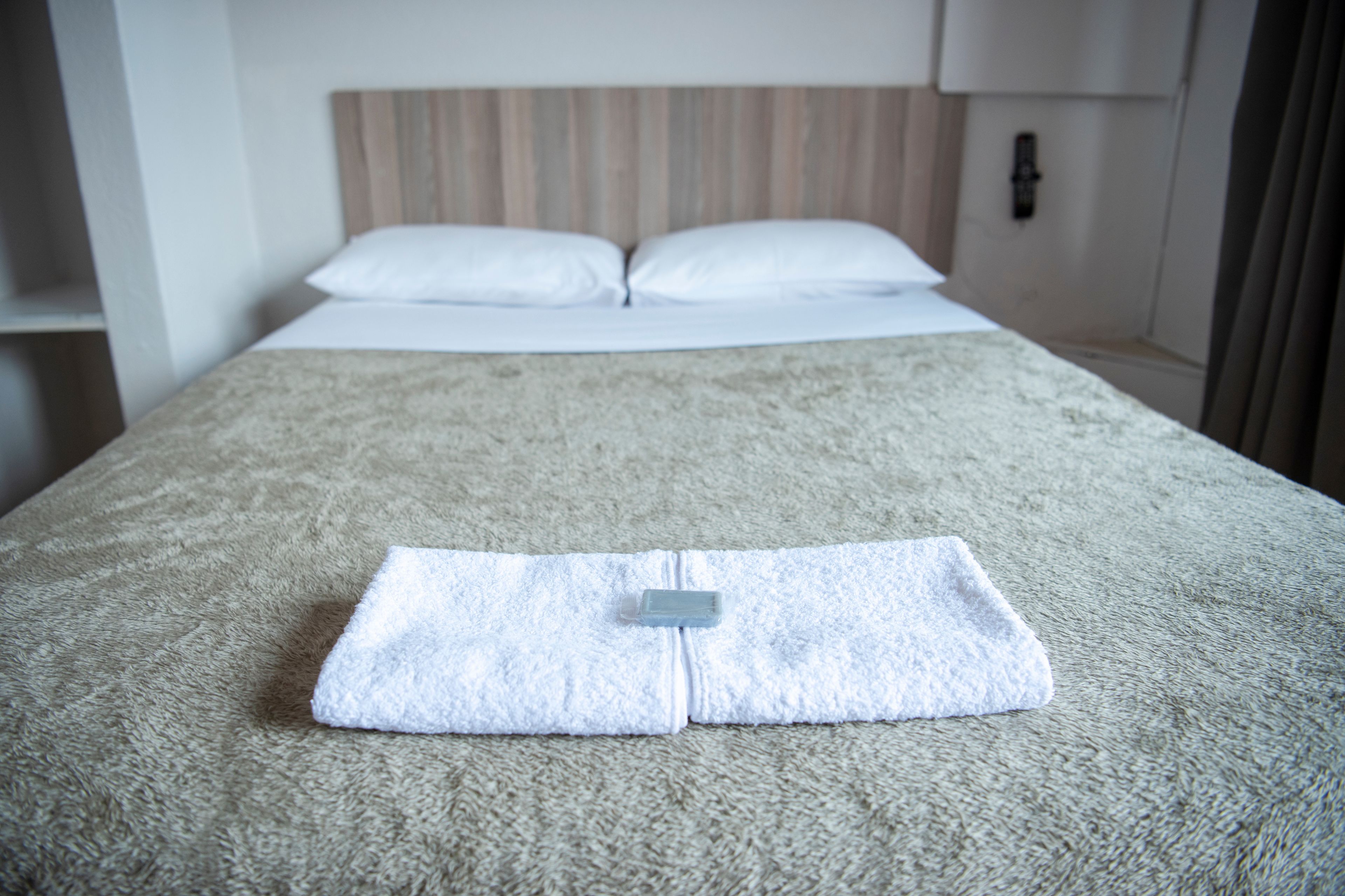 Cama bem arrumada com toalha dobrada e controle remoto sobre o lençol.