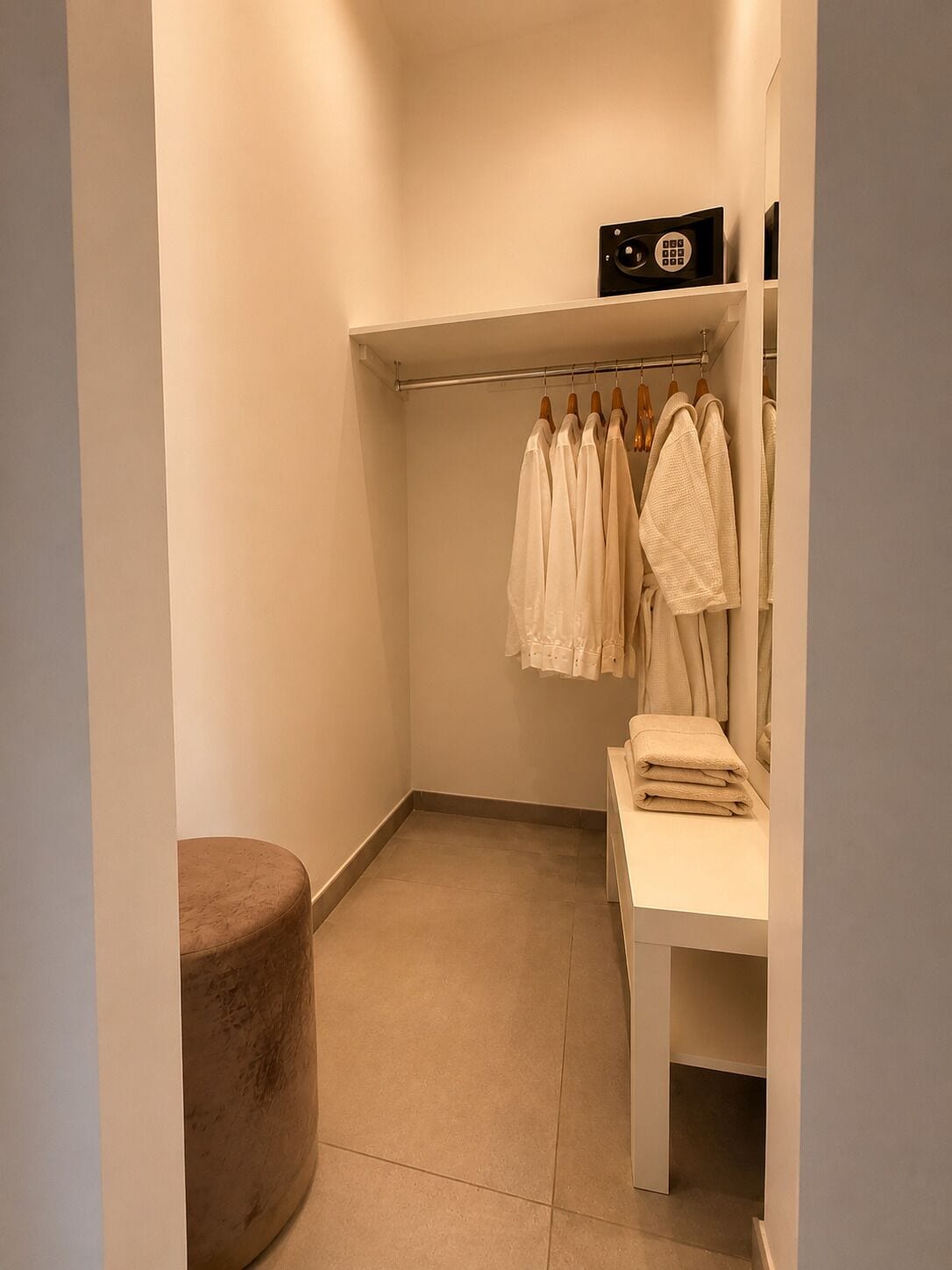 Um closet amplo com roupões pendurados, um banquinho e uma prateleira com toalhas dobradas.