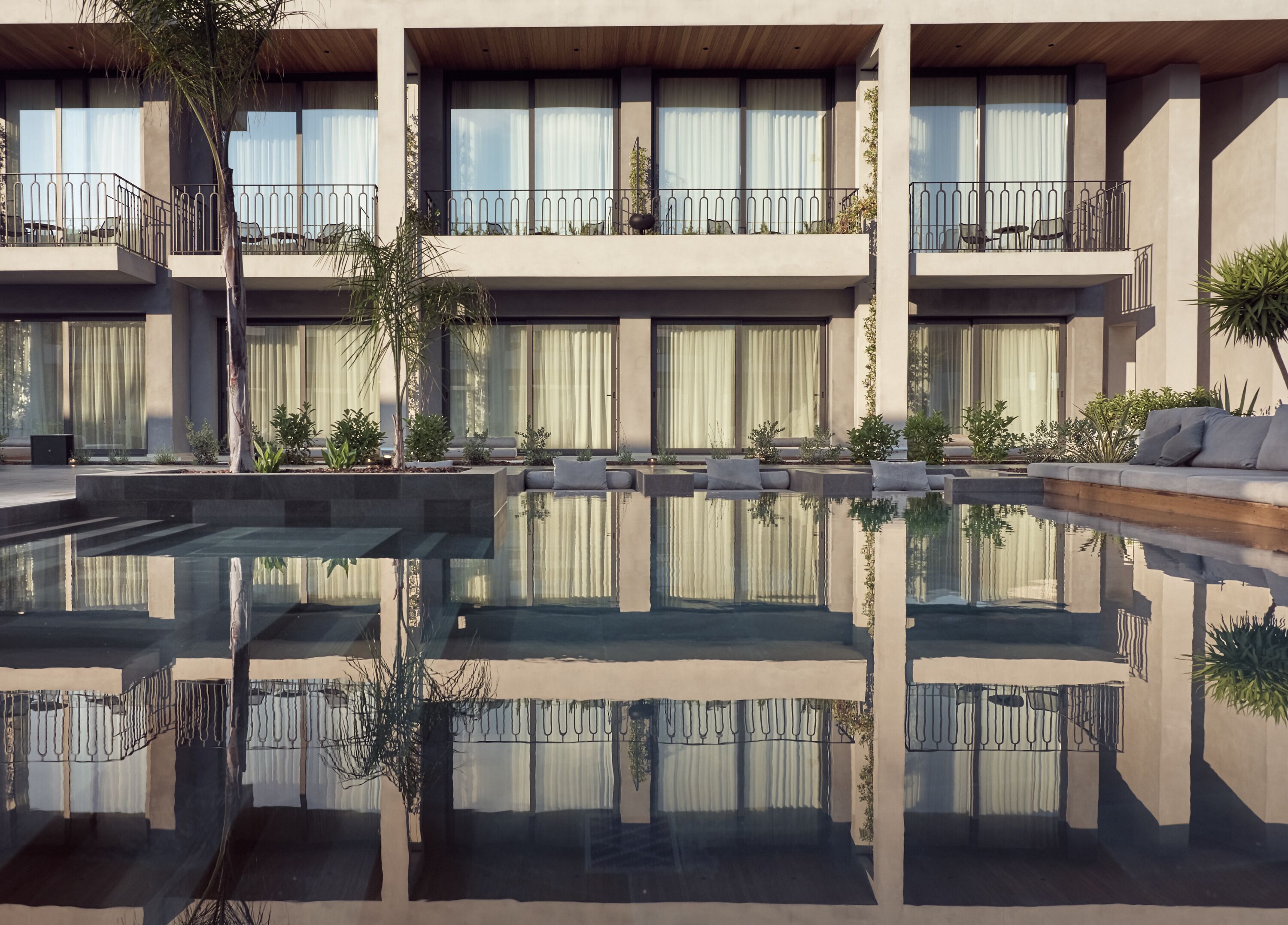 Um hotel moderno com uma grande piscina espelhada, várias varandas e paisagismo exuberante.