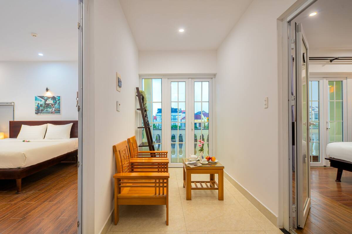 Quarto de hotel com cama, cadeiras de madeira, uma mesinha com um vaso e um quadro na parede.