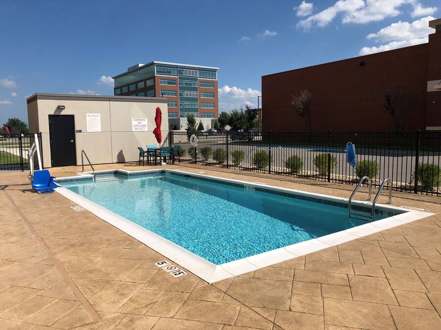 Uma piscina retangular com água azul cristalina, cercada por um deck ladrilhado e uma cerca de metal preto.