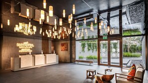 Um hall de hotel moderno com balcão de recepção, luminárias pendentes e área de estar com sofá e banquetas.