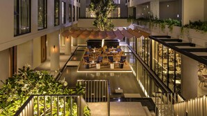 Um átrio moderno de hotel, com área de estar central, guarda-corpos de vidro e plantas em interior.