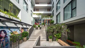 Um edifício moderno com uma escadaria central, várias varandas com plantas e um mural na parede esquerda.