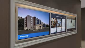 Um ecrã digital emoldurado mostra um hotel com fachada de edifício moderno, entrada com jardim e placa a indicar 'SPRINGHILL SUITES BY MARRIOTT'.