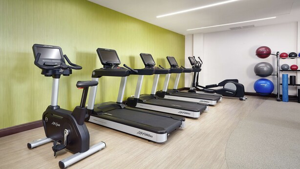 Vários esteiras numa ginásio com parede verde e bolas de exercício em suporte.