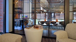 Um interior moderno com uma ampla janela de vidro, um banquinho branco e uma área de estar com sofá e poltronas.