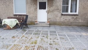 Uma casa com um pátio ladrilhado, uma mesa com cadeiras, uma porta e uma janela.