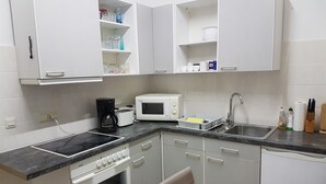 Cozinha compacta com armários brancos, micro-ondas, cafeteira e pia.