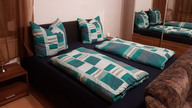 Um quarto com cama, travesseiros, mesa de cabeceira, espelho e um quadro na parede.