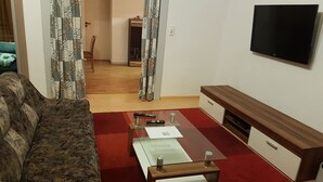 Sala de estar com sofá, mesa de centro de vidro, televisão de tela plana e um armário de madeira.