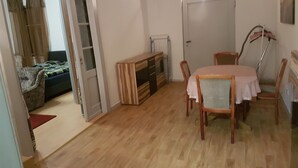 Quarto com mesa de jantar, cadeiras, um banco, guarda-roupa e porta que dá para outro cômodo.