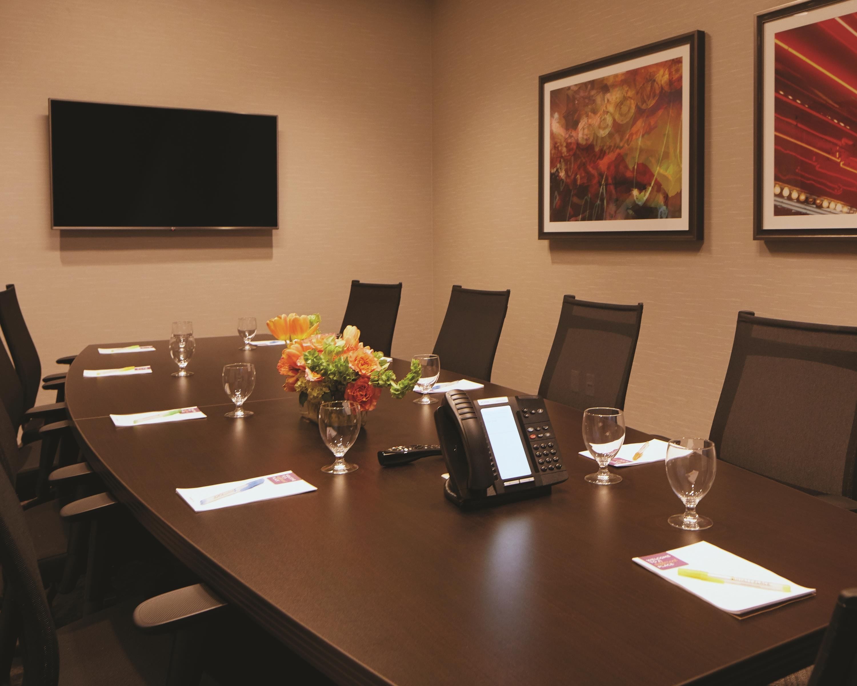 Uma sala de conferências com uma mesa comprida, cadeiras, um telefone e um vaso de flores.