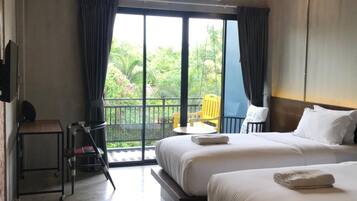 Quarto de hotel com duas camas, uma mesinha, uma cadeira e varanda com vista para vegetação.